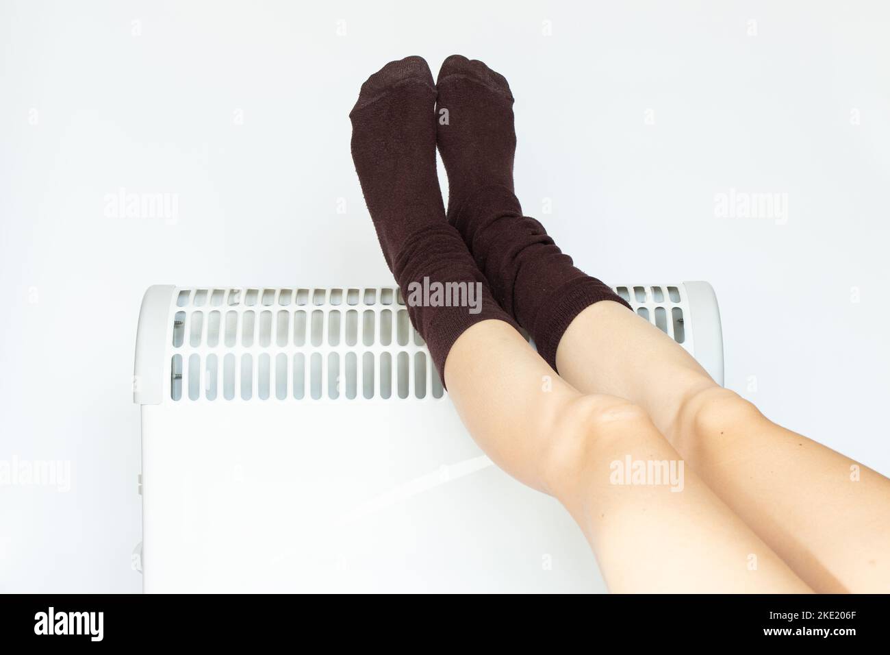 Women's legs in socks on an electric convector on a white background, a ...