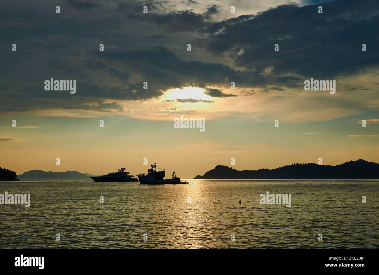 A scenic view of silhouettes of boats sailing in the ocean at sunset in ...