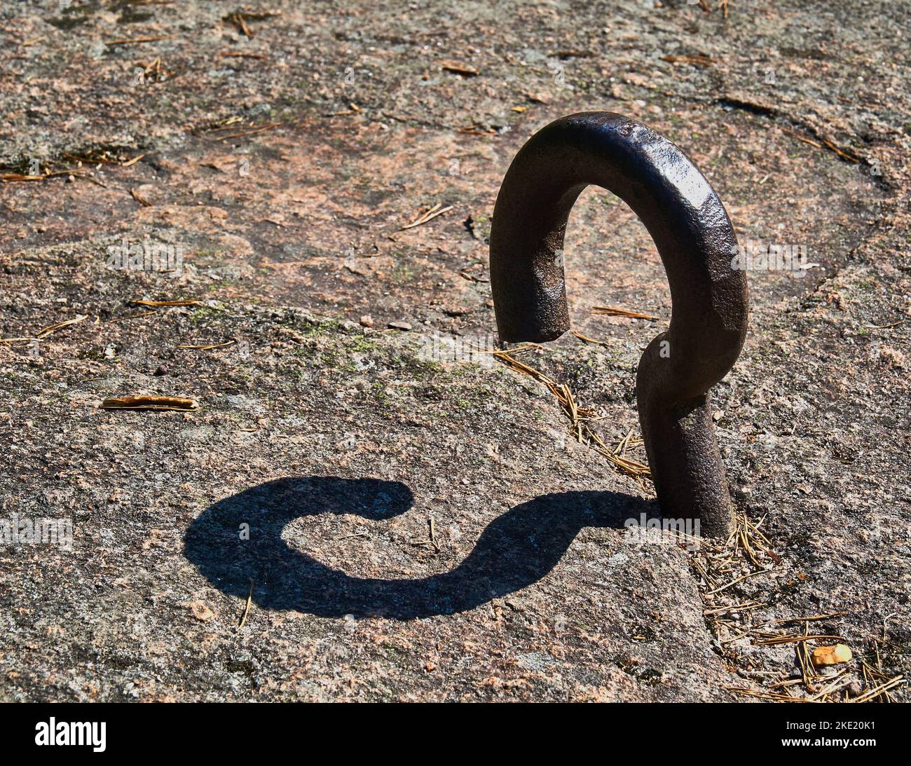 A closeup shot of an old metal hook with its shadow on the ground in ...