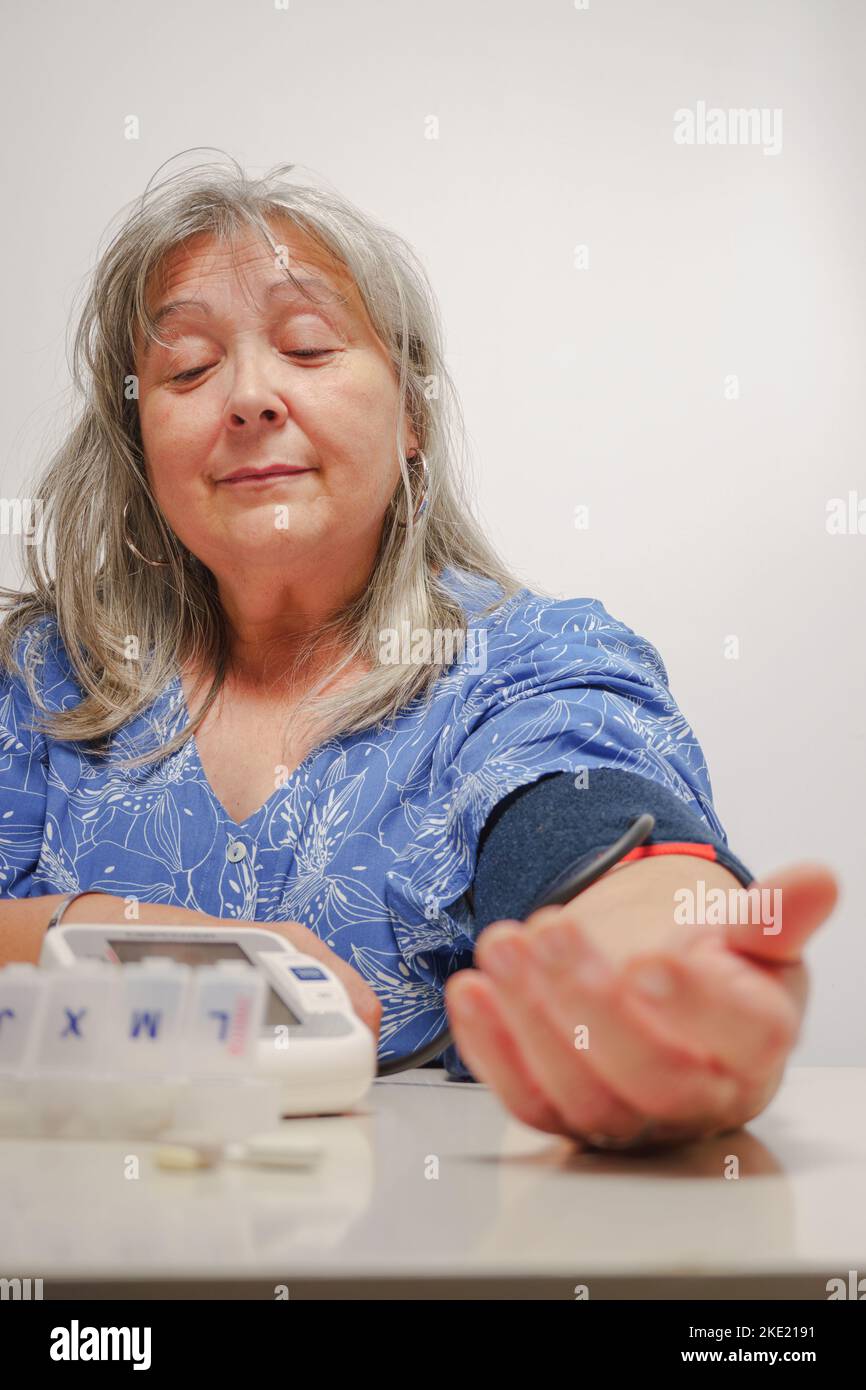older white-haired woman with glasses taking her blood pressure at home ...