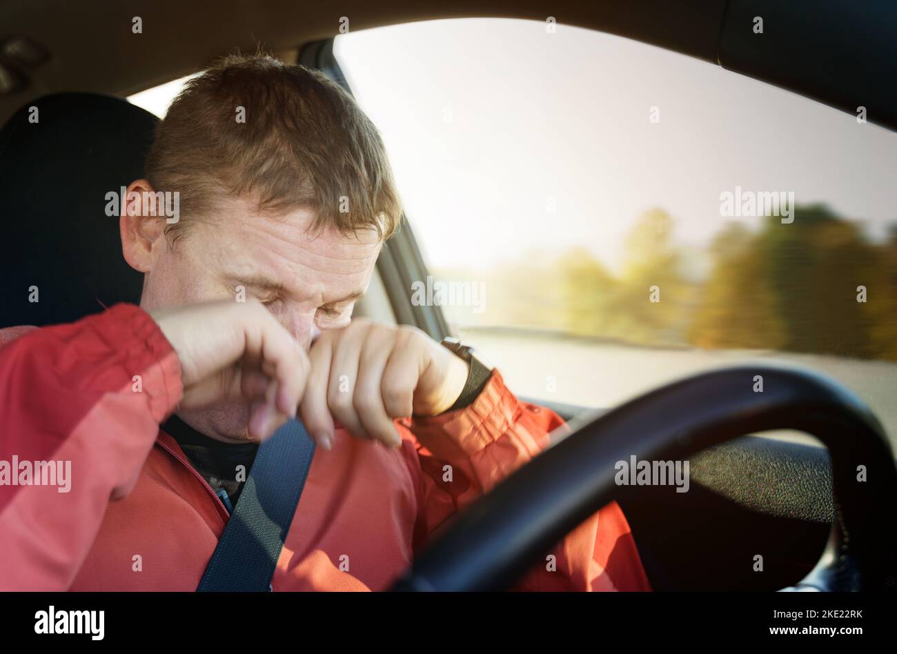 A tired driver rubs his eyelids with his hands while driving while ...