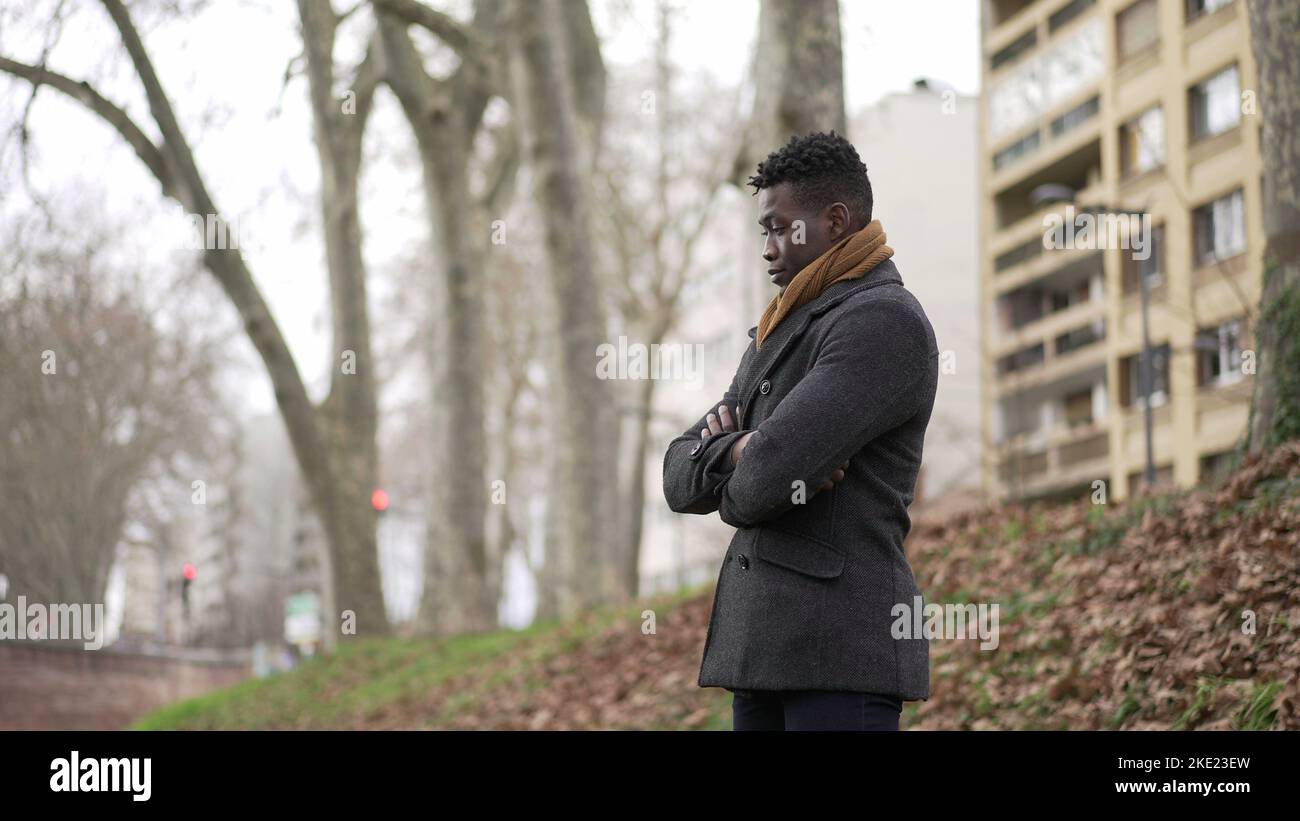 Black man arms crossed standing outside at park thinking wearing winter ...
