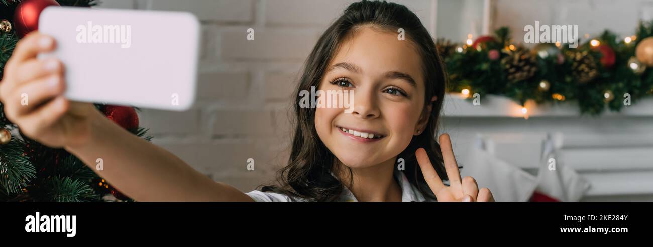 Positive child showing peace sign while taking selfie during Christmas ...