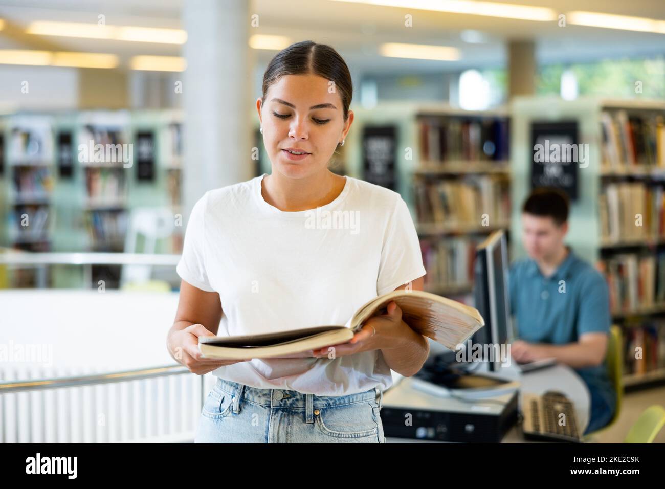 Smiling student girl standing in the university library, holding textbooks in hands Stock Photo ...