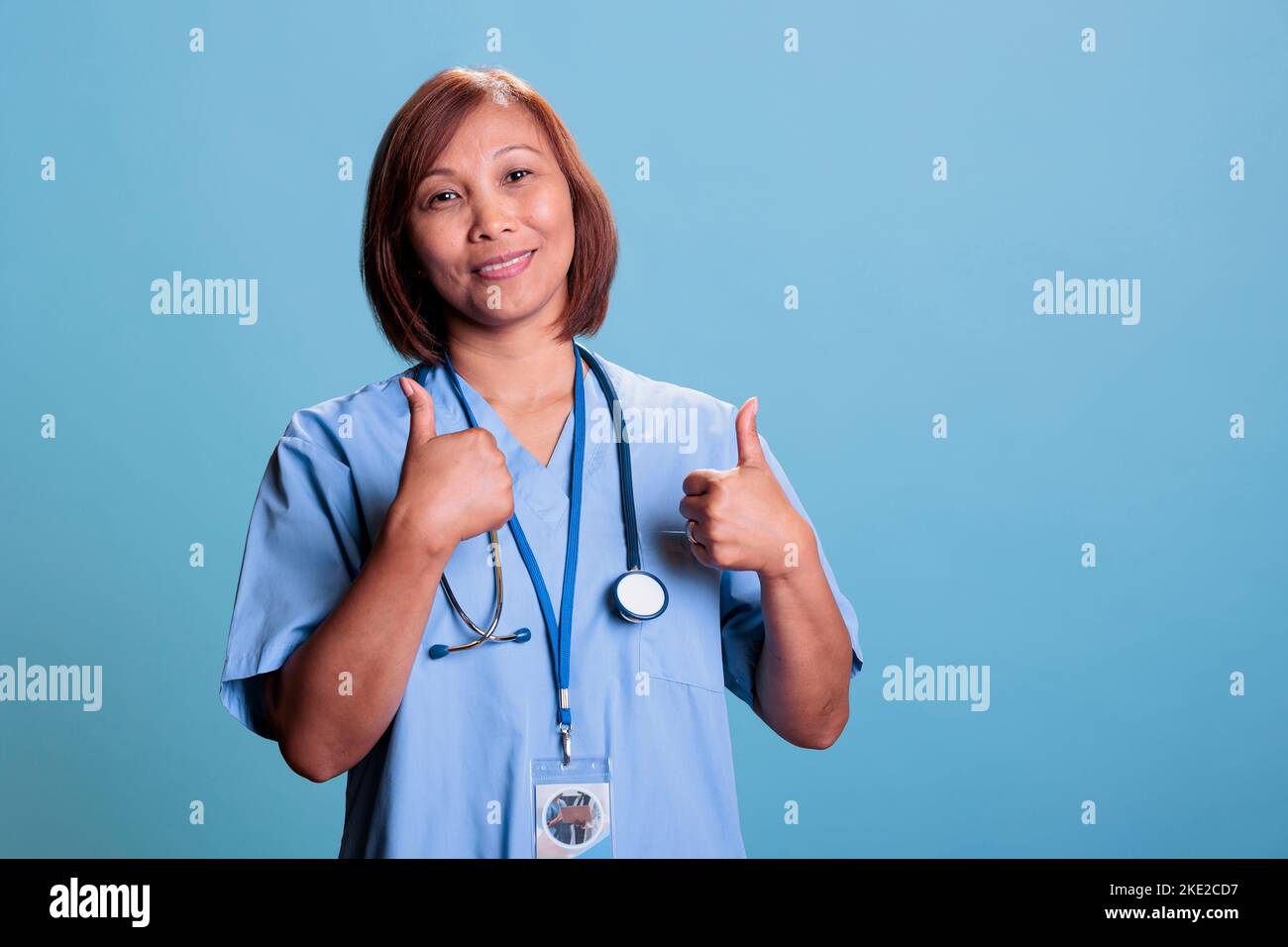 Positive medical assistant with stethoscope smiling at camera while ...