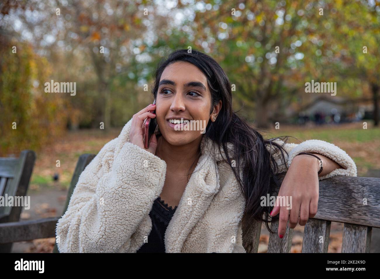 Attractive indian girl sitting on a bench at a london park having a ...