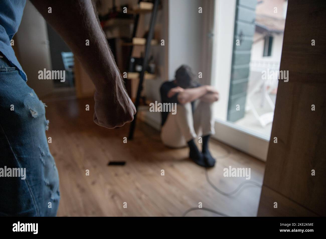 Man huddled on the floor where the shadow of another person standing ...
