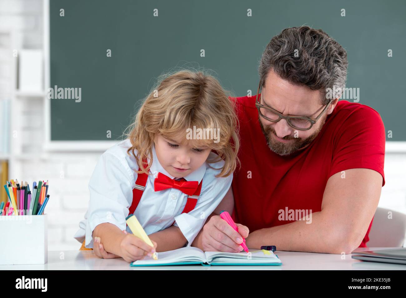Teacher helping child student pupil from elementary school in classroom ...