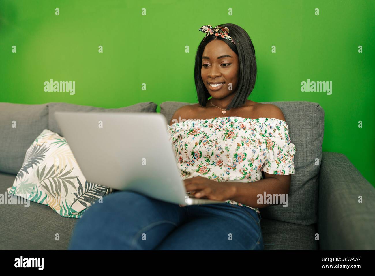 Young african woman working on laptop computer at home sitting on sofa ...