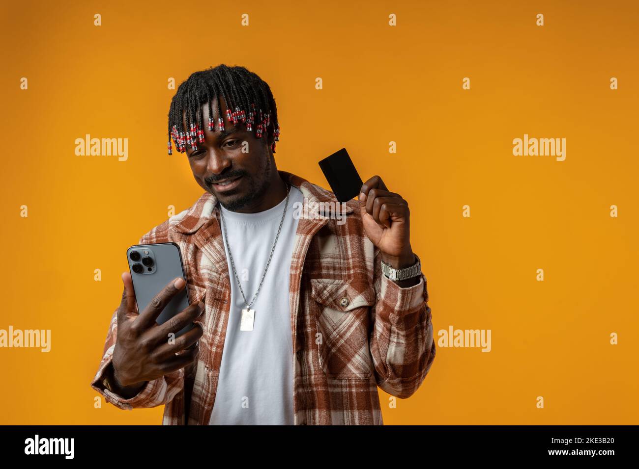 Smiling young african man on yellow background using mobile phone and ...