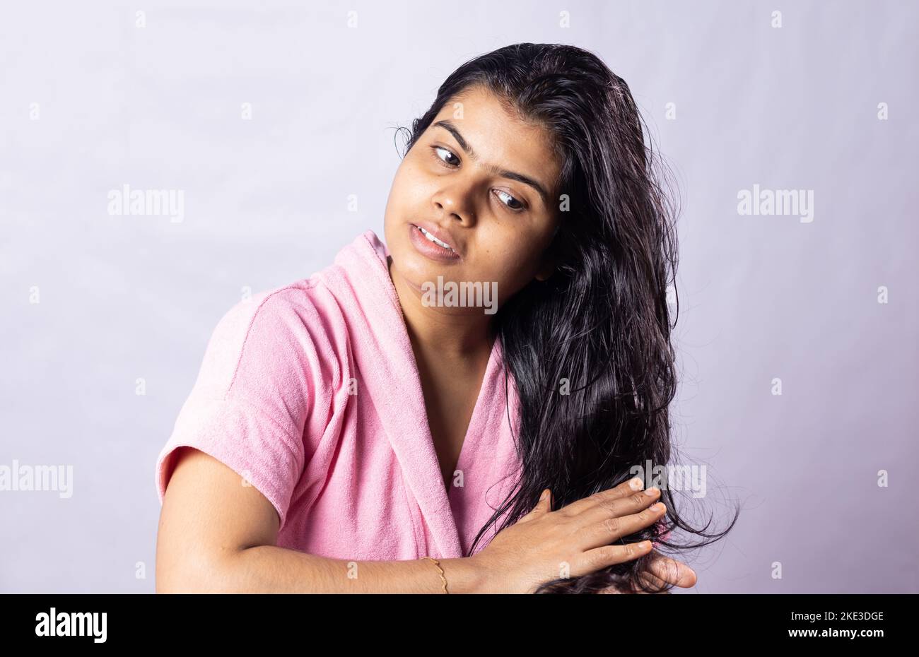 A beautiful Indian woman applying hair oil on her black hair with smile ...