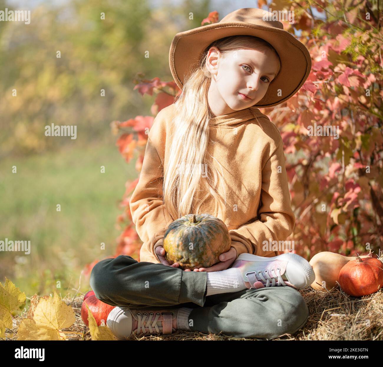 Little girls sitting among hay bales and pumpkins in the autumn garden ...