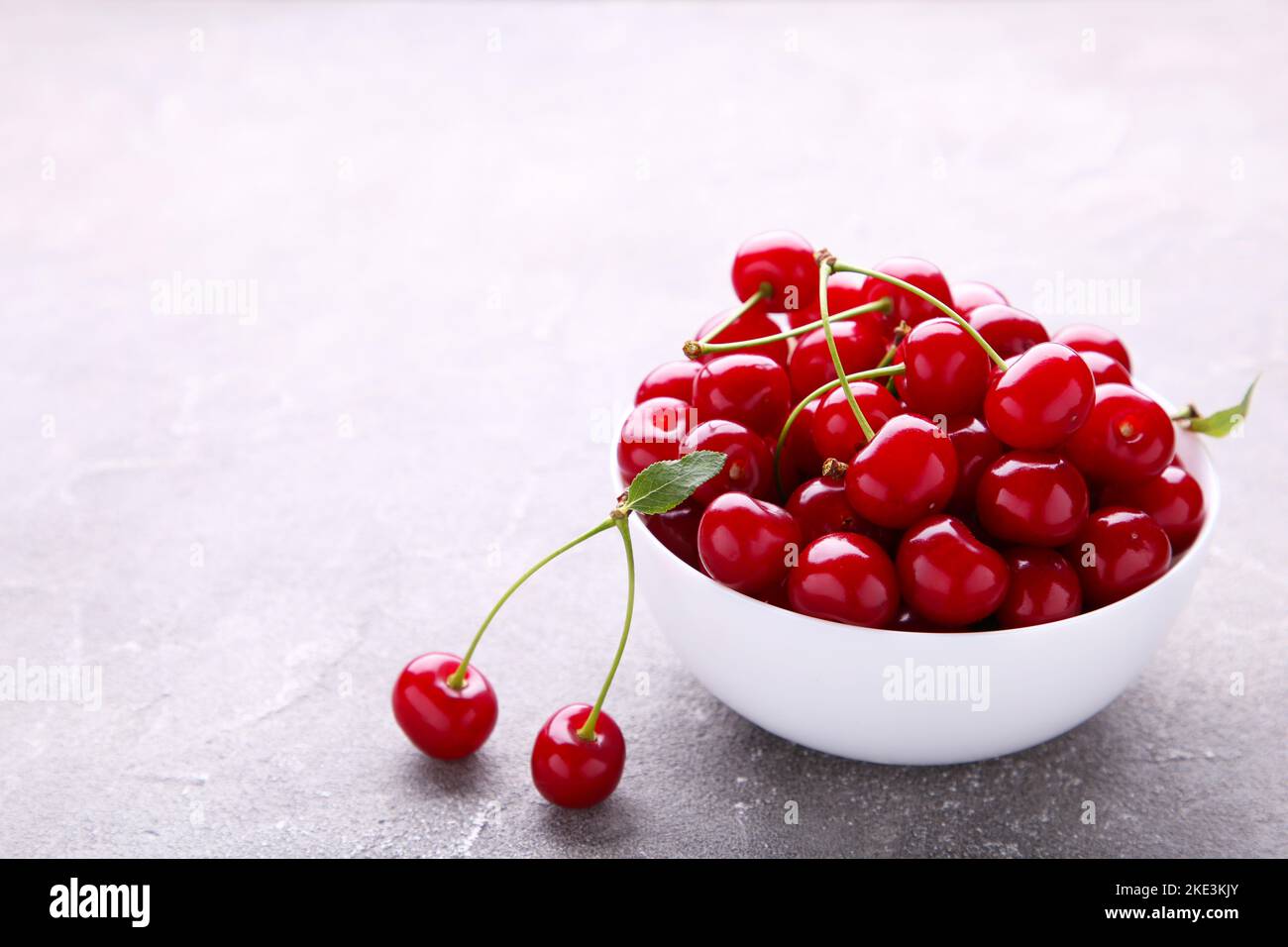 Fresh red cherry fruit in plate on grey background Stock Photo - Alamy