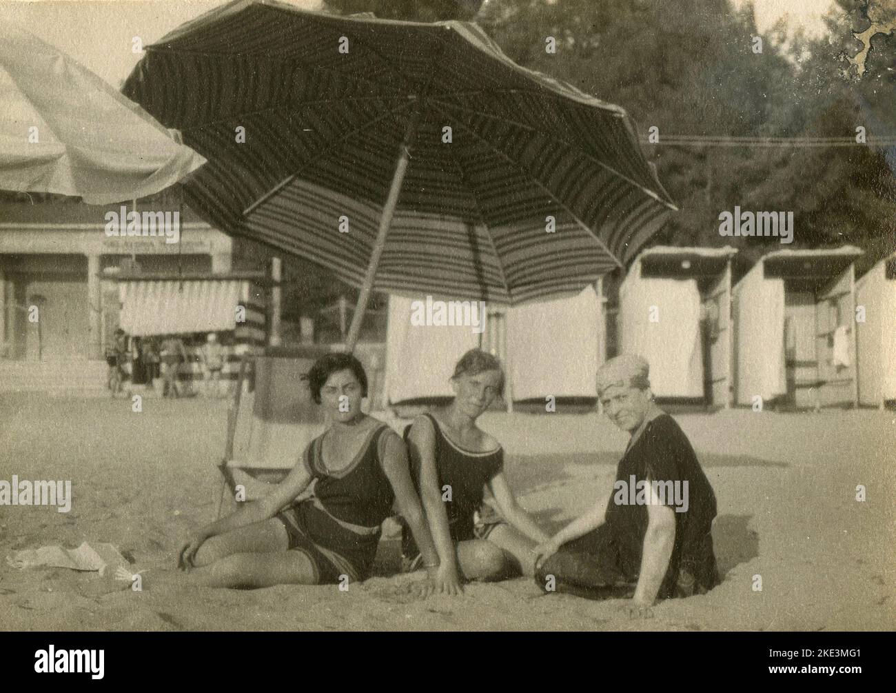 Three women at the beach under the umbrella with full swimming suite ...
