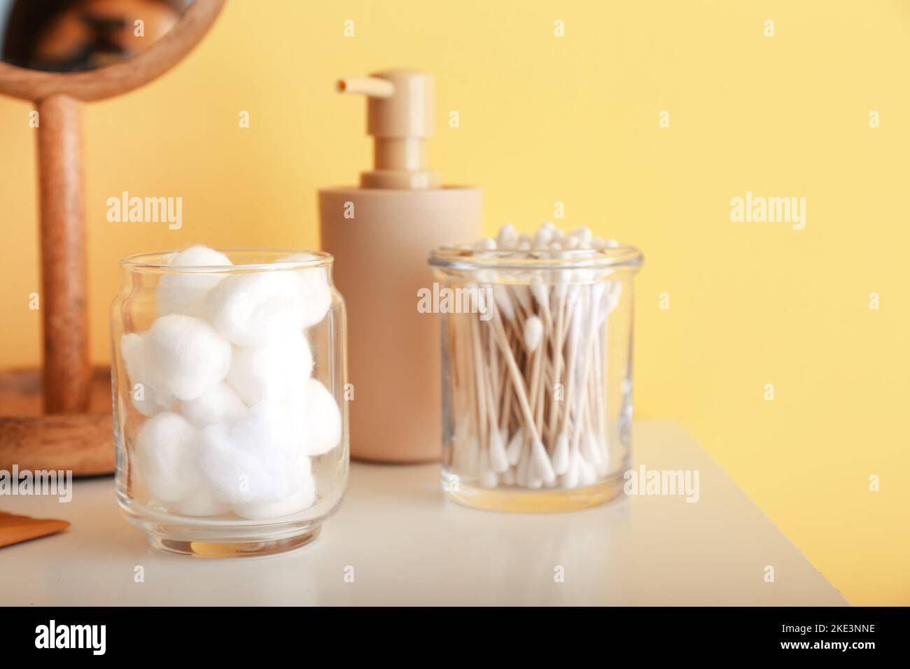 Container with soft cotton wool and swabs on table near yellow wall ...