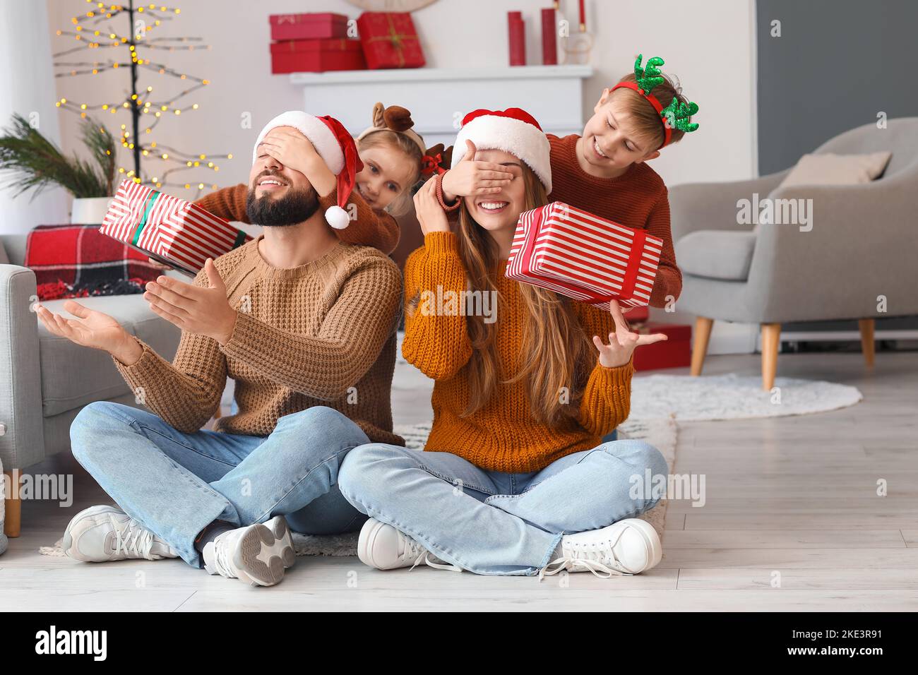Happy little children surprising their parents with Christmas gifts at ...