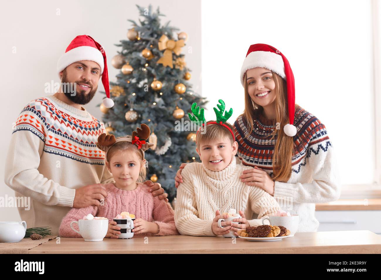Happy parents with their little children and cups of cocoa in kitchen ...