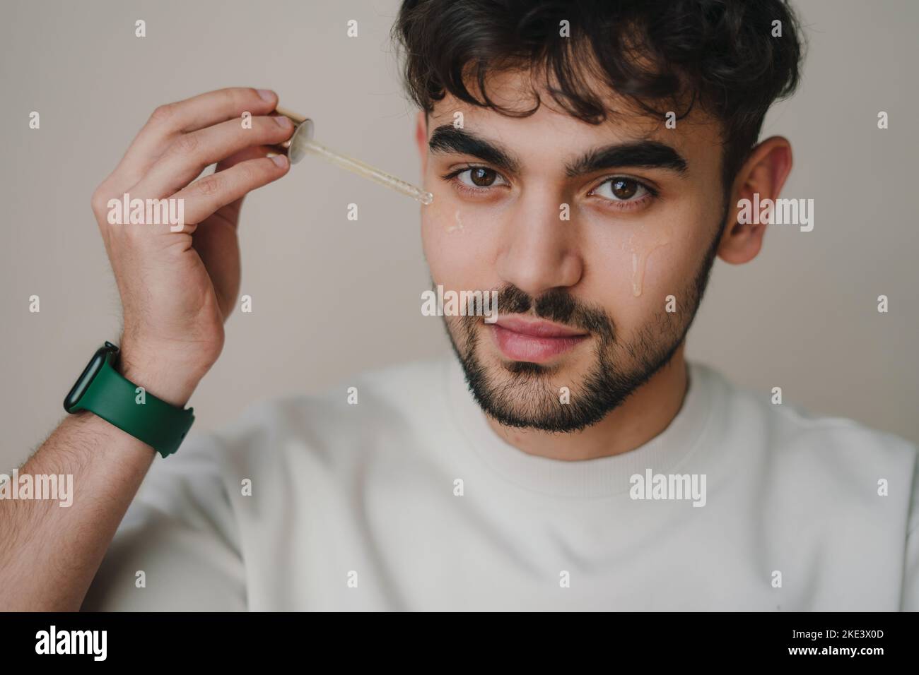 Handsome man applying moisturizing serum on face, isolated over grey ...