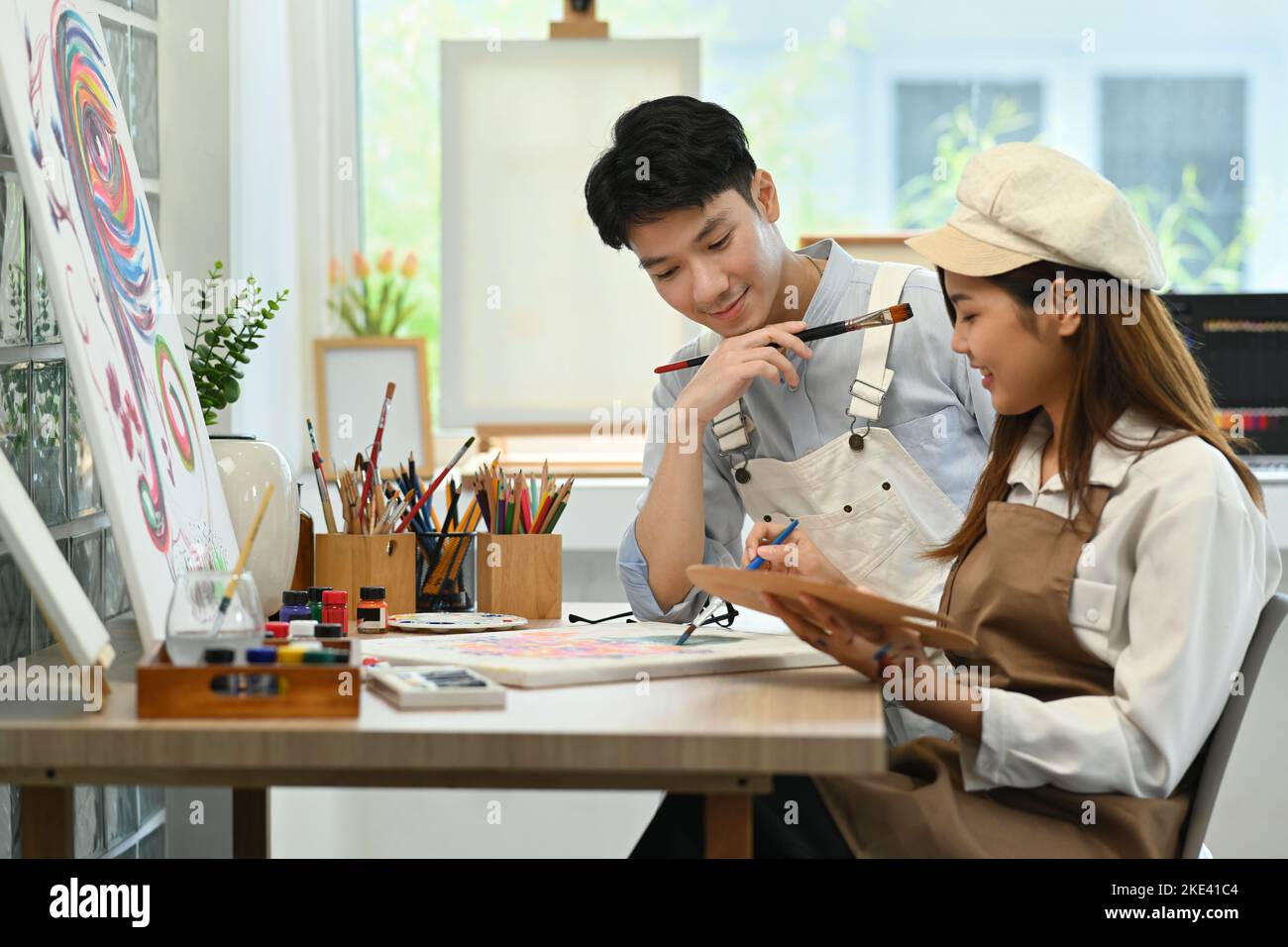 Young asian male artist and his girlfriend painting together at bright ...