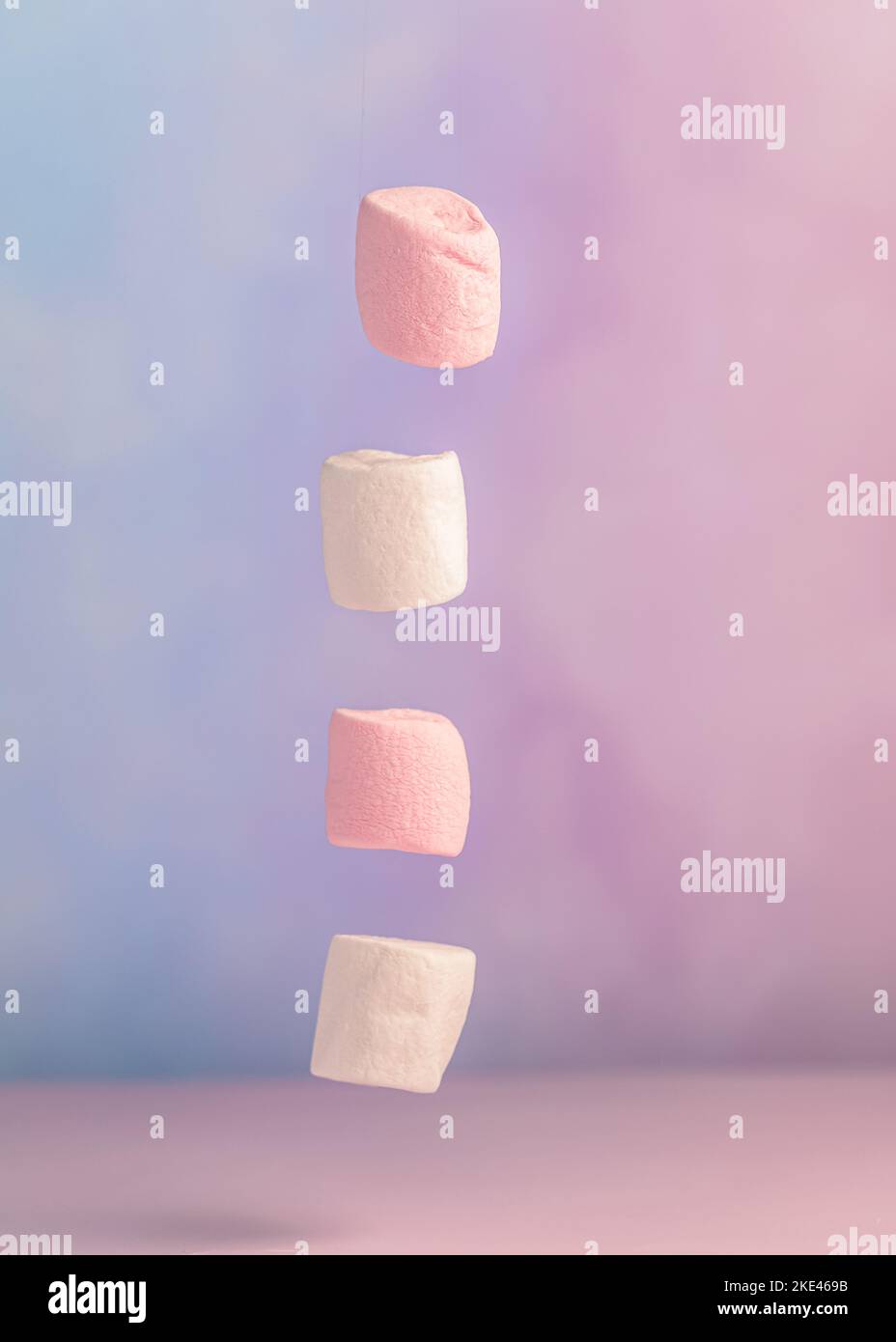 A vertical shot of floating marshmallows against a pink and purple ...