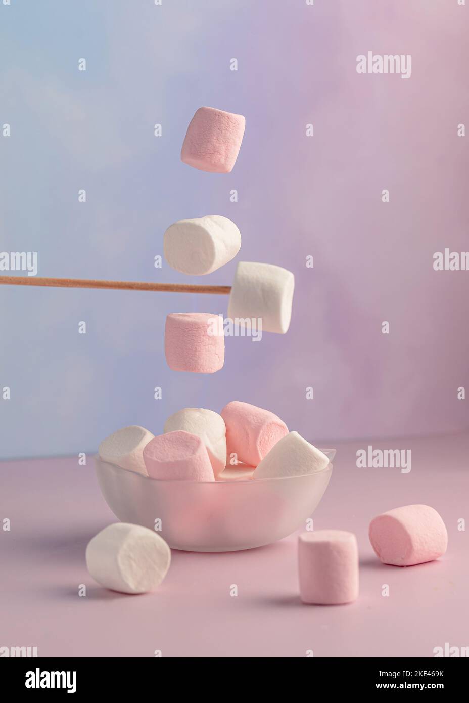 A vertical shot of floating marshmallows over a bowl against a pink and ...