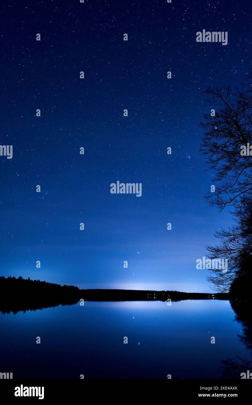 A mesmerizing starry night sky over a pond reflecting on the water ...