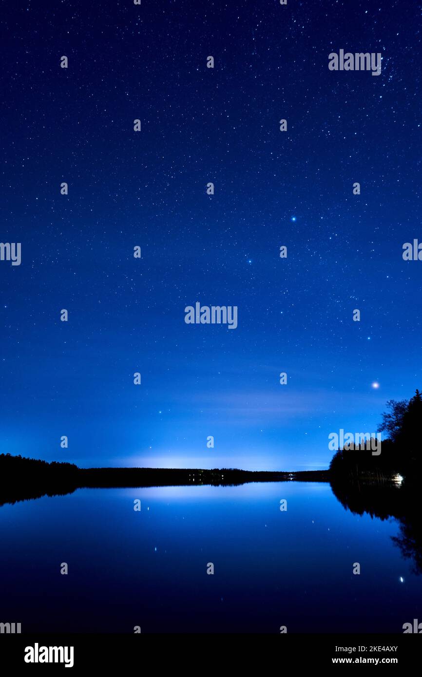 A mesmerizing starry night sky over a pond reflecting on the water ...