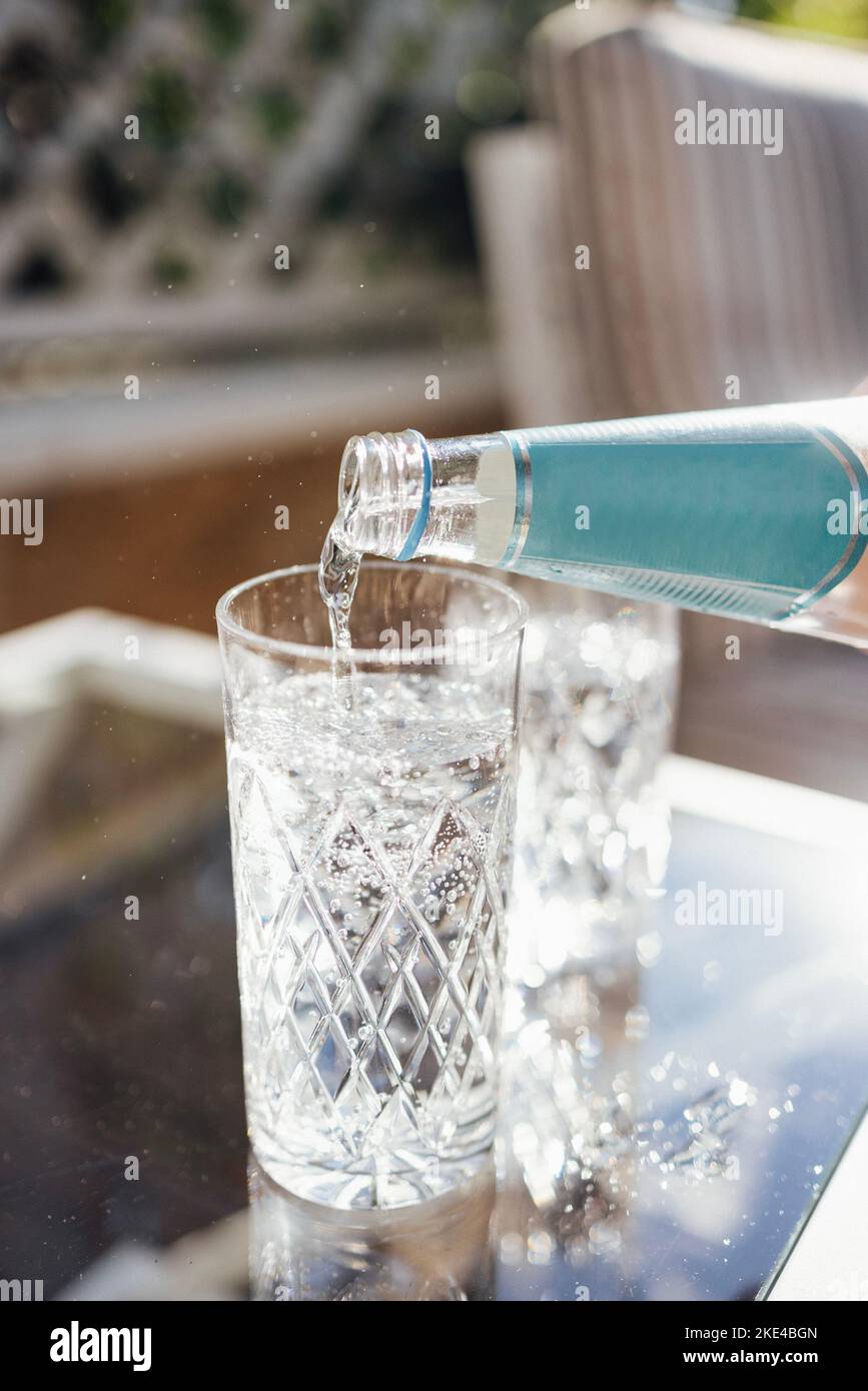 Pouring sparkling water from the bottle into glass. Water drink pouring into glass, garden ...