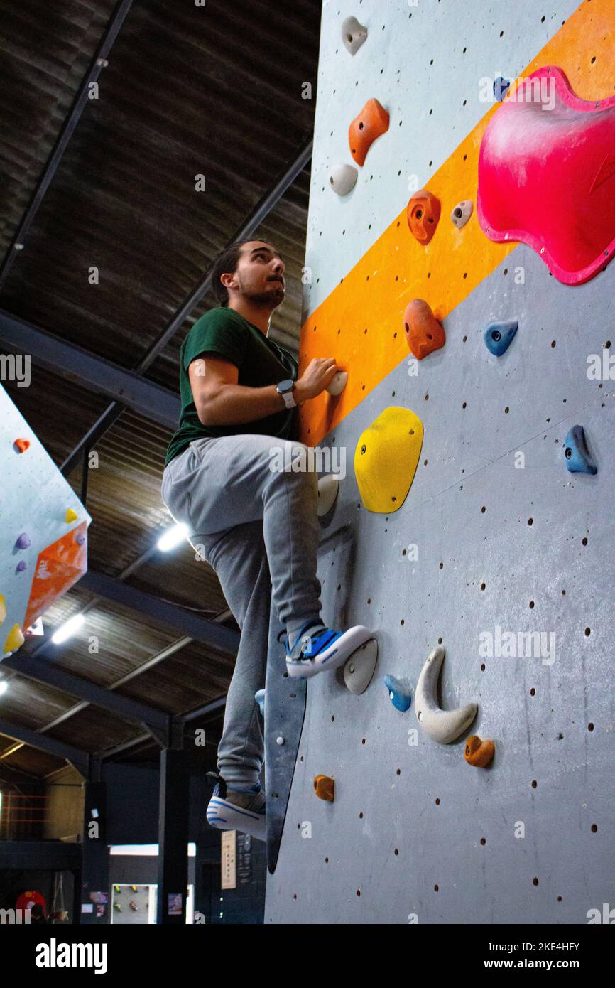 A handsome rock-climber male going up on colorful slopers on bouldering ...
