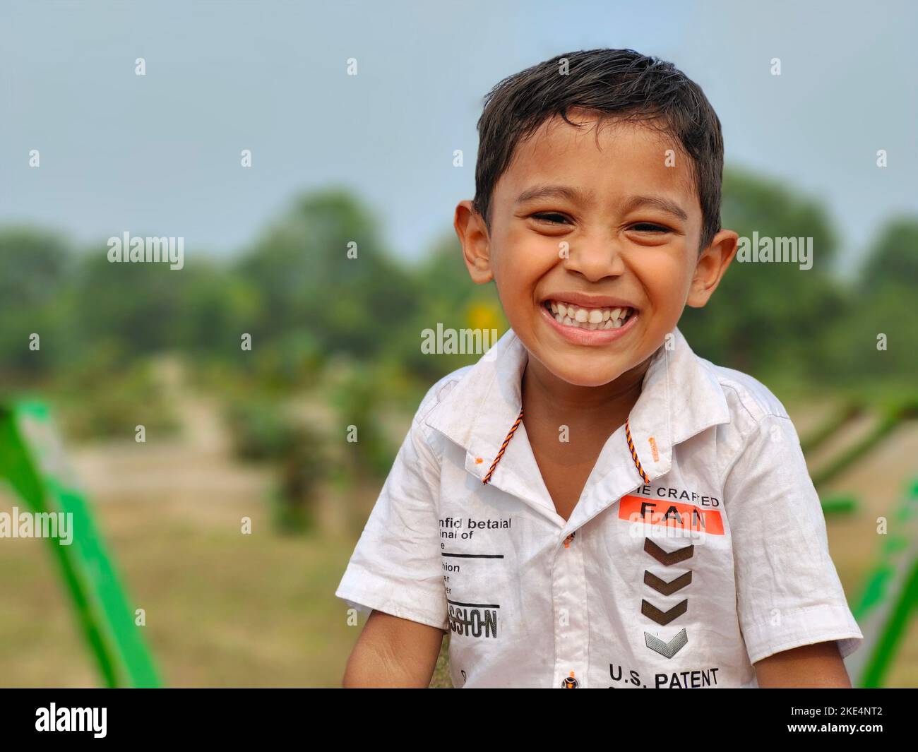 A portrait of a young Indian boy laughing while looking at the camera ...