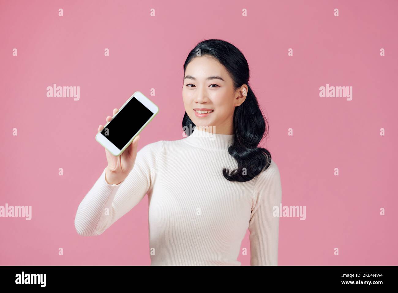Beautiful Asian woman holding blank screen smartphone on pink ...