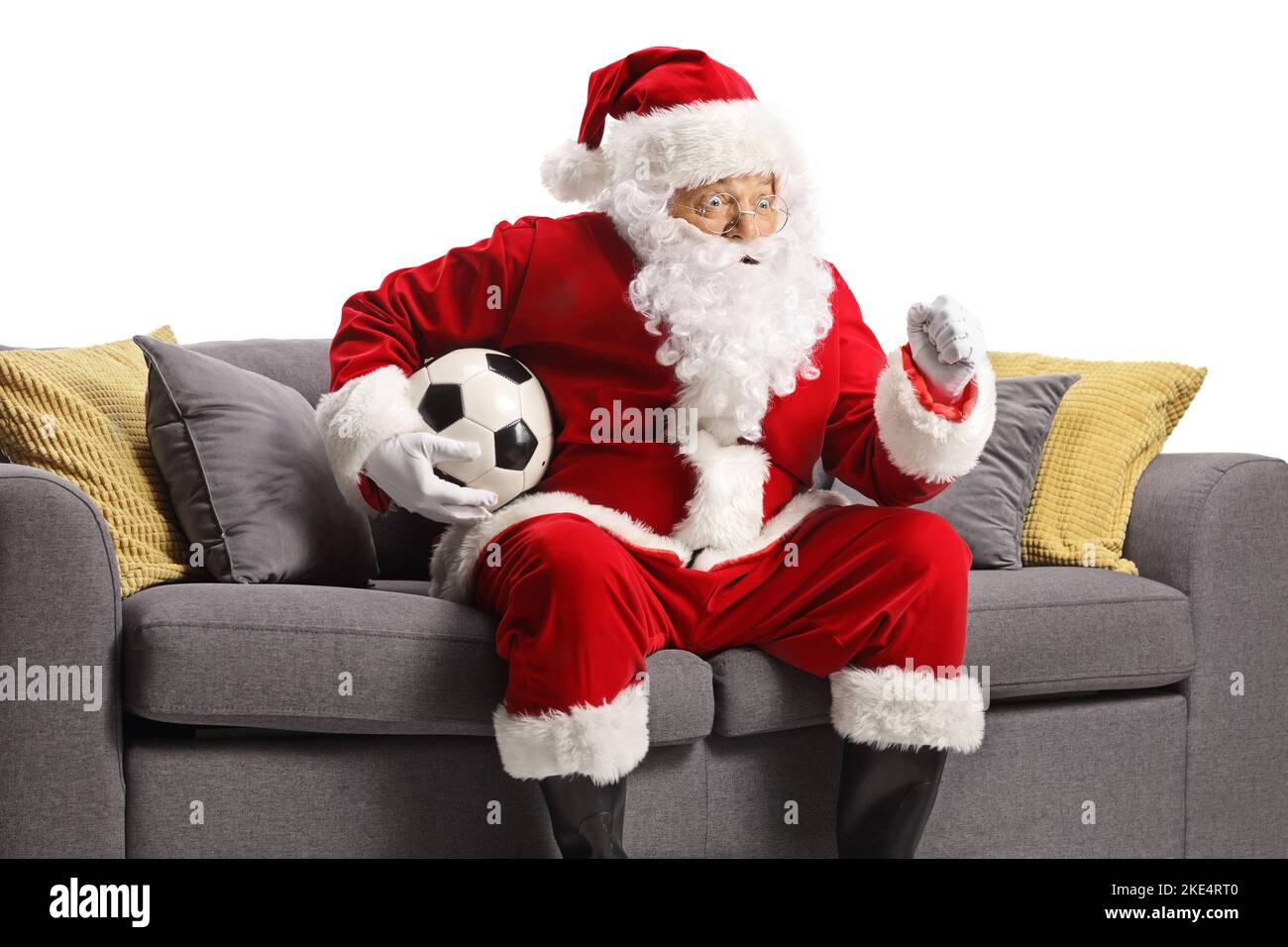 Santa claus cheering, holding a football and sitting on a sofa isolated ...