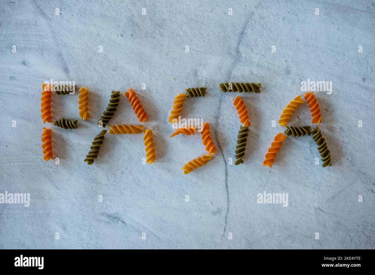 Word pasta spelled out in fuselli pasta that is tricolor and uncooked ...