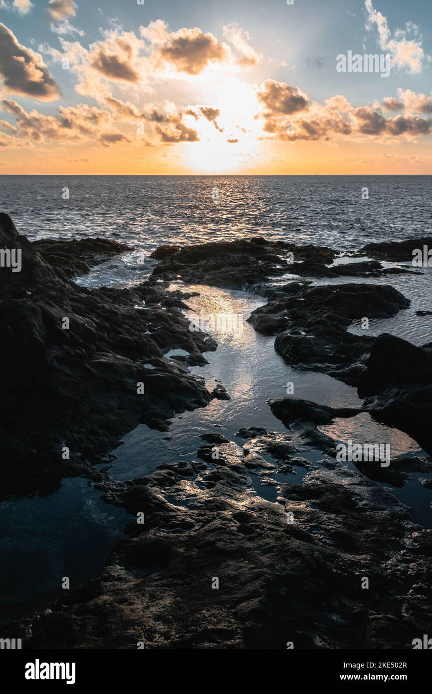 A vertical shot of a rocky coastline with a cloudy sunset sky in the ...
