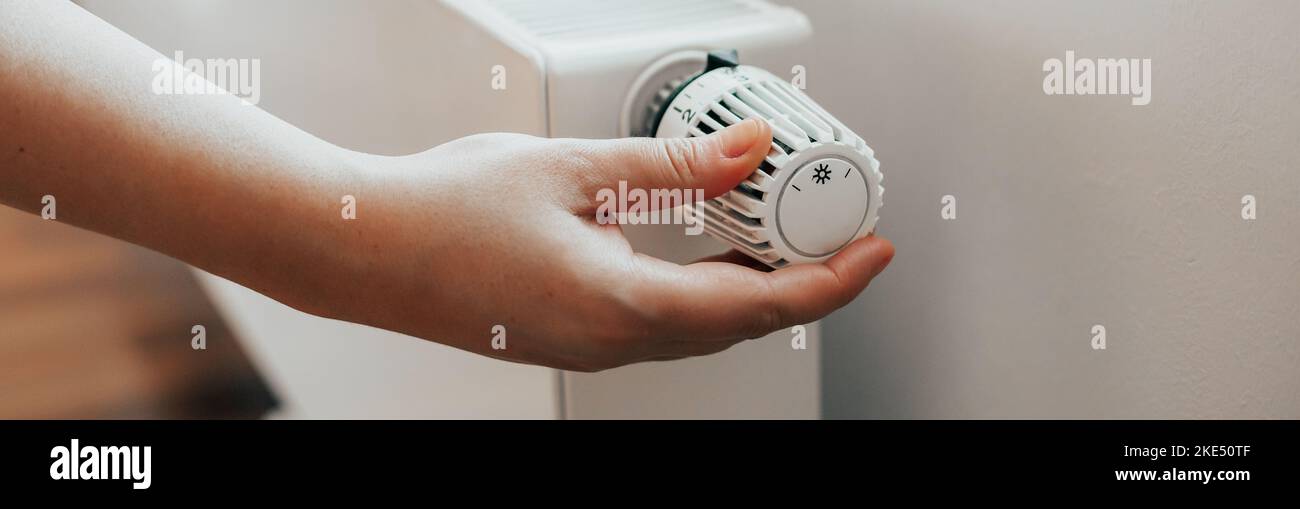 Close up og woman hand regulating heating on the radiator during winter ...