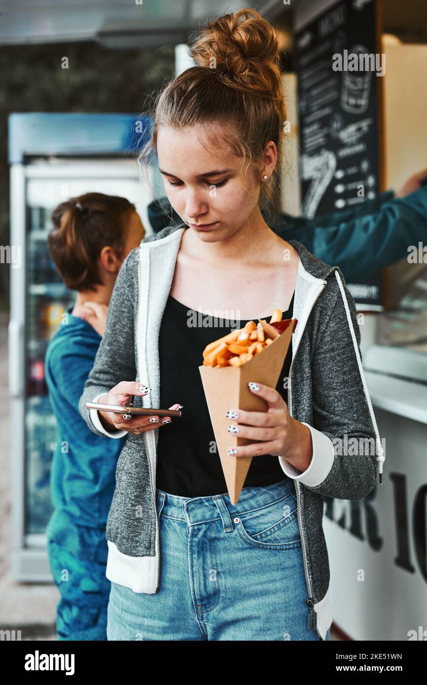 Teenage Girl Eating Potato Fries From Carton Cone Standing In Front Of