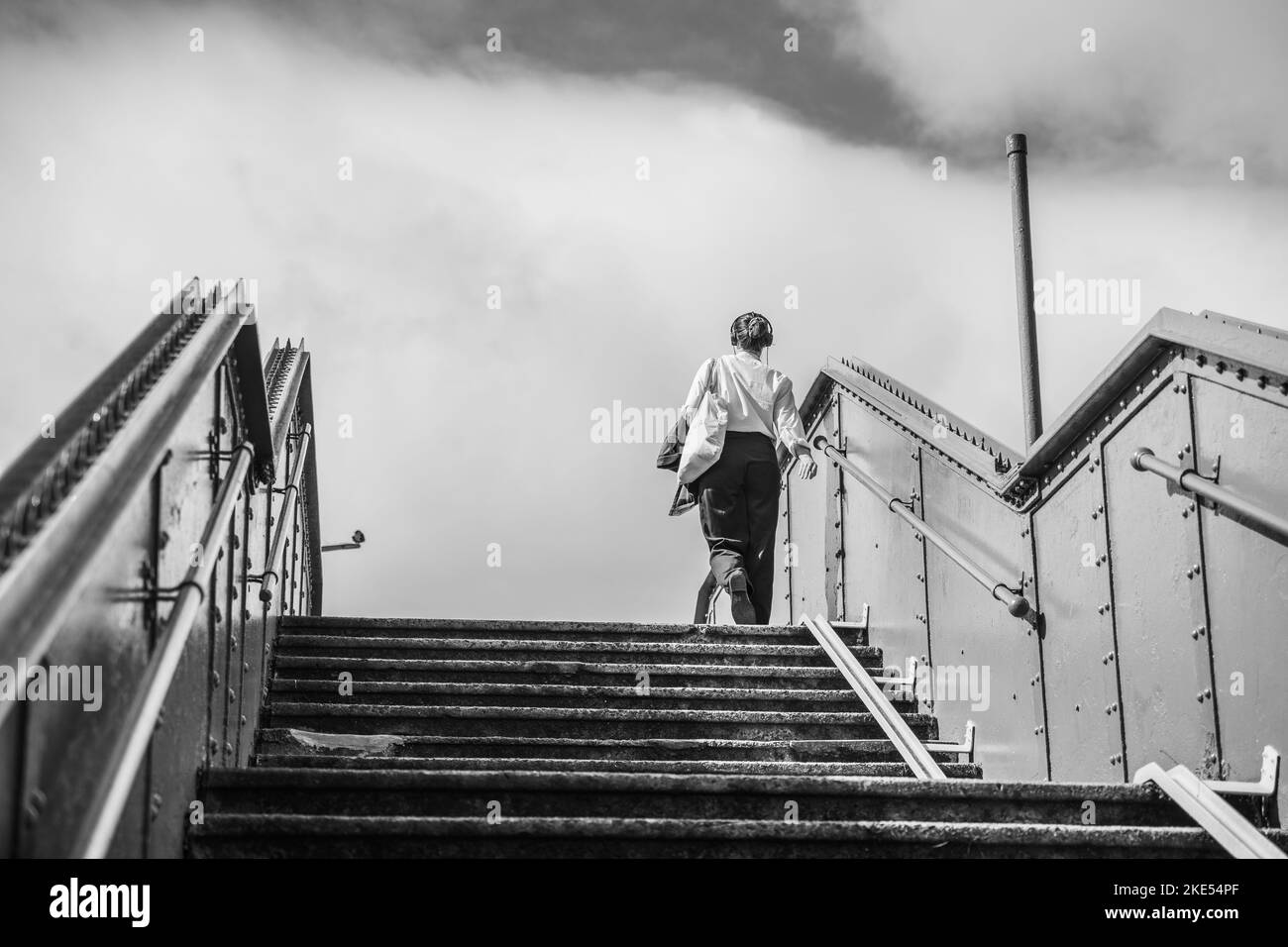 A low-angle grayscale of a woman walking over a steel and concrete ...