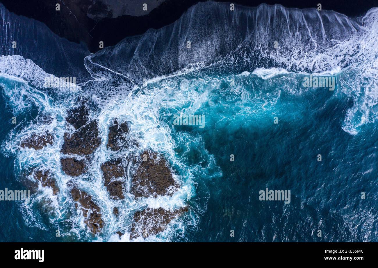 the turquoise ocean breaks in white foamy waves on the black beach ...
