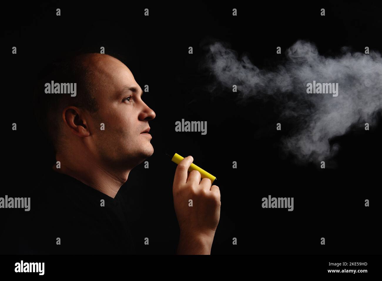 A young man smokes an electronic cigarette against a black background ...