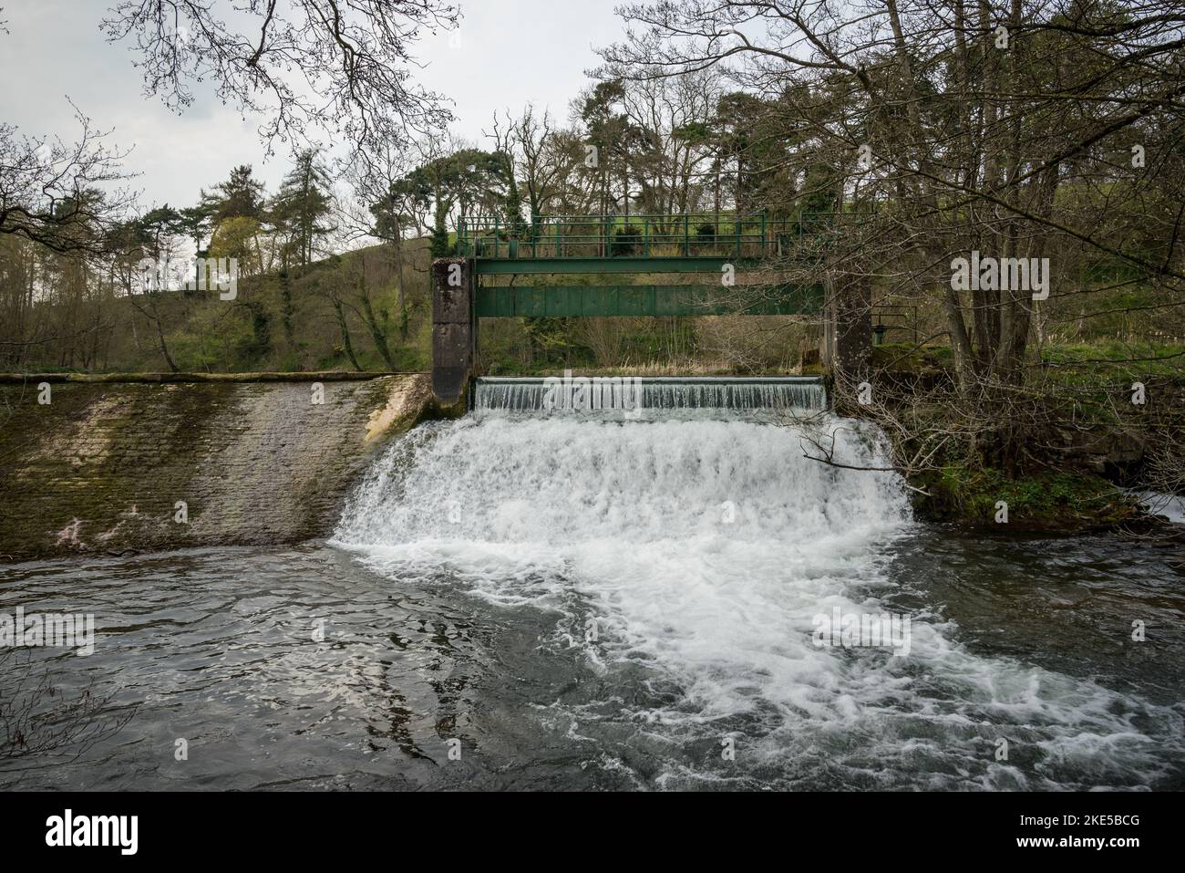 A small dam with overflowing water with a forest on the background ...