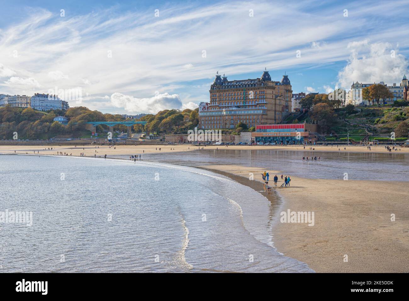 A tideline curves across a sandy beach and people enjoy the seaside ...