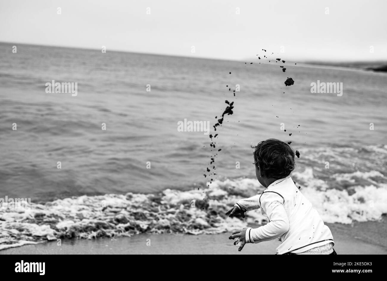 Young child in a swimsuit throwing sand into open water Stock Photo - Alamy