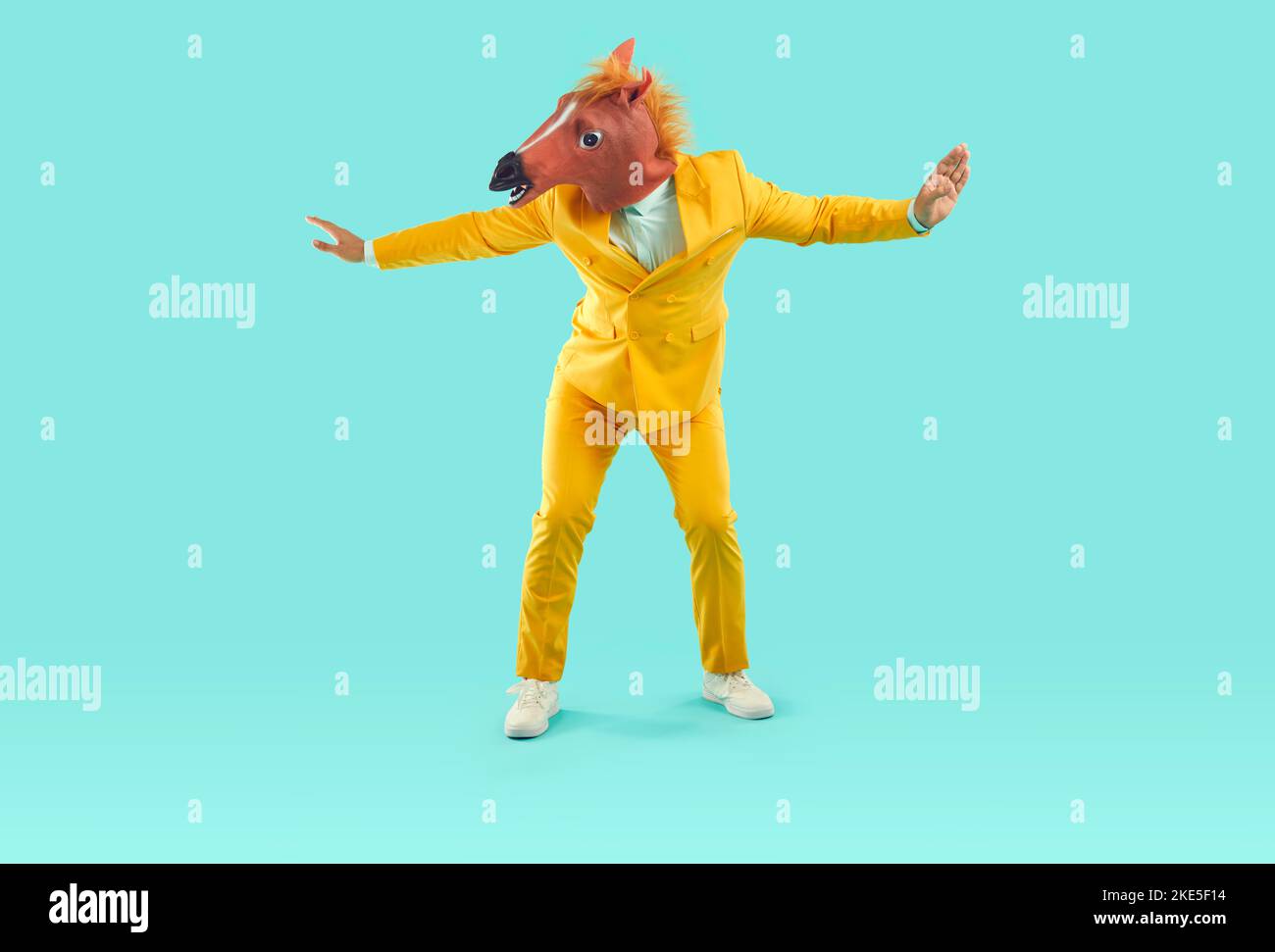 Funny happy man in yellow suit and horse mask dancing on turquoise ...