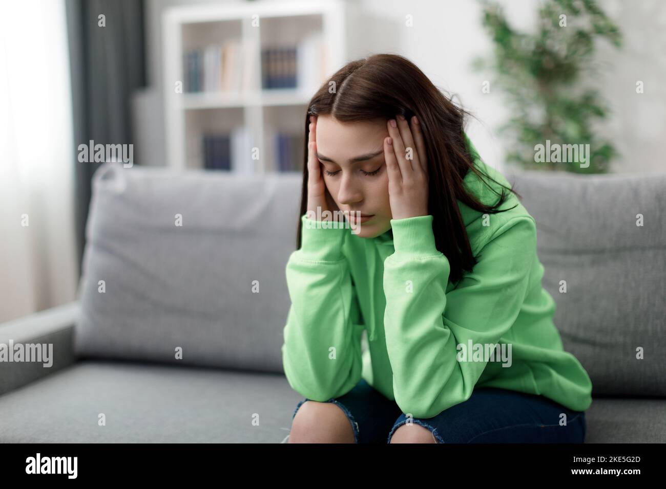 Tired stressed woman with brown hair sitting on comfy couch and holding ...