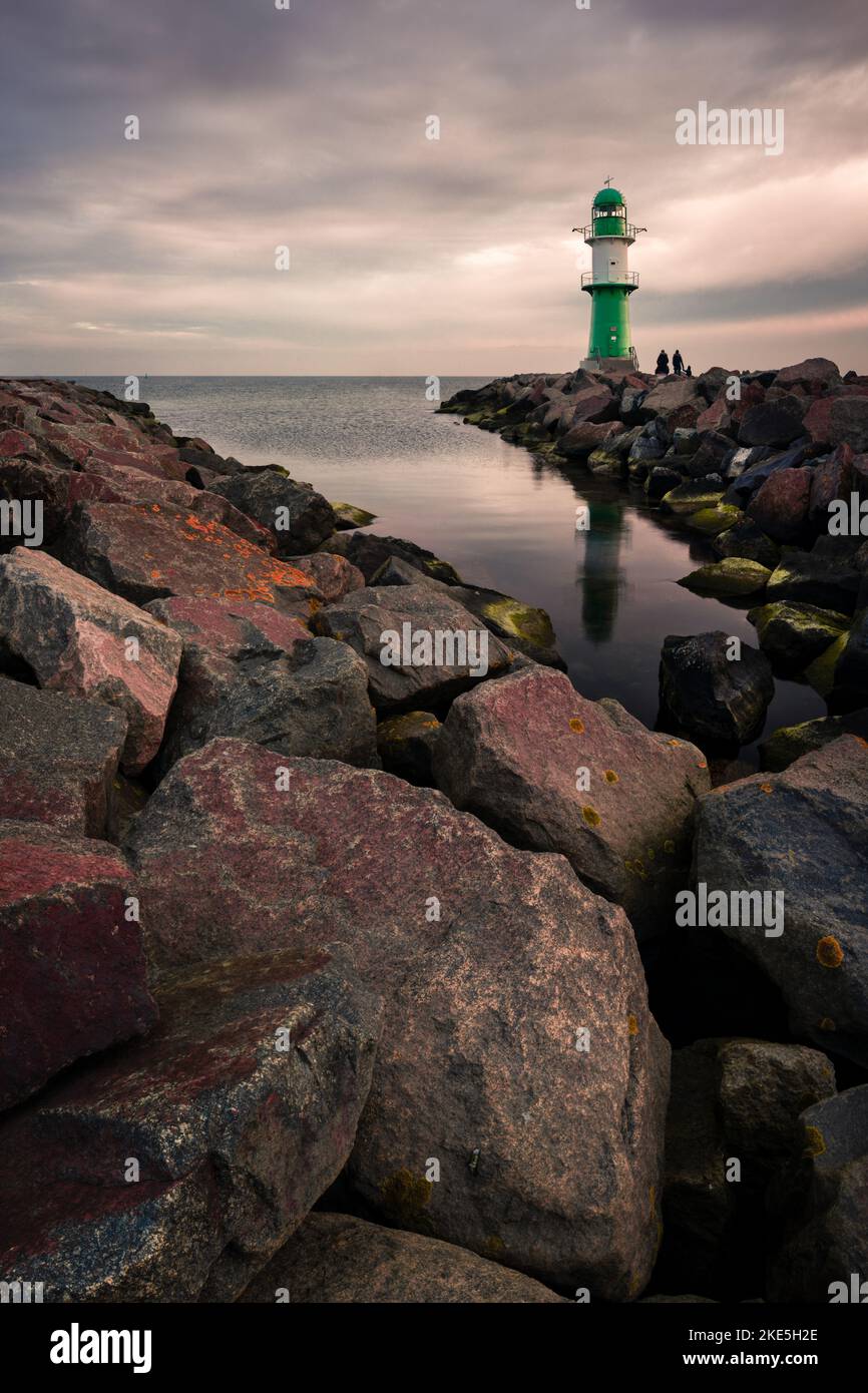 A vertical shot of a green lighthouse on the coast in cloudy sky ...