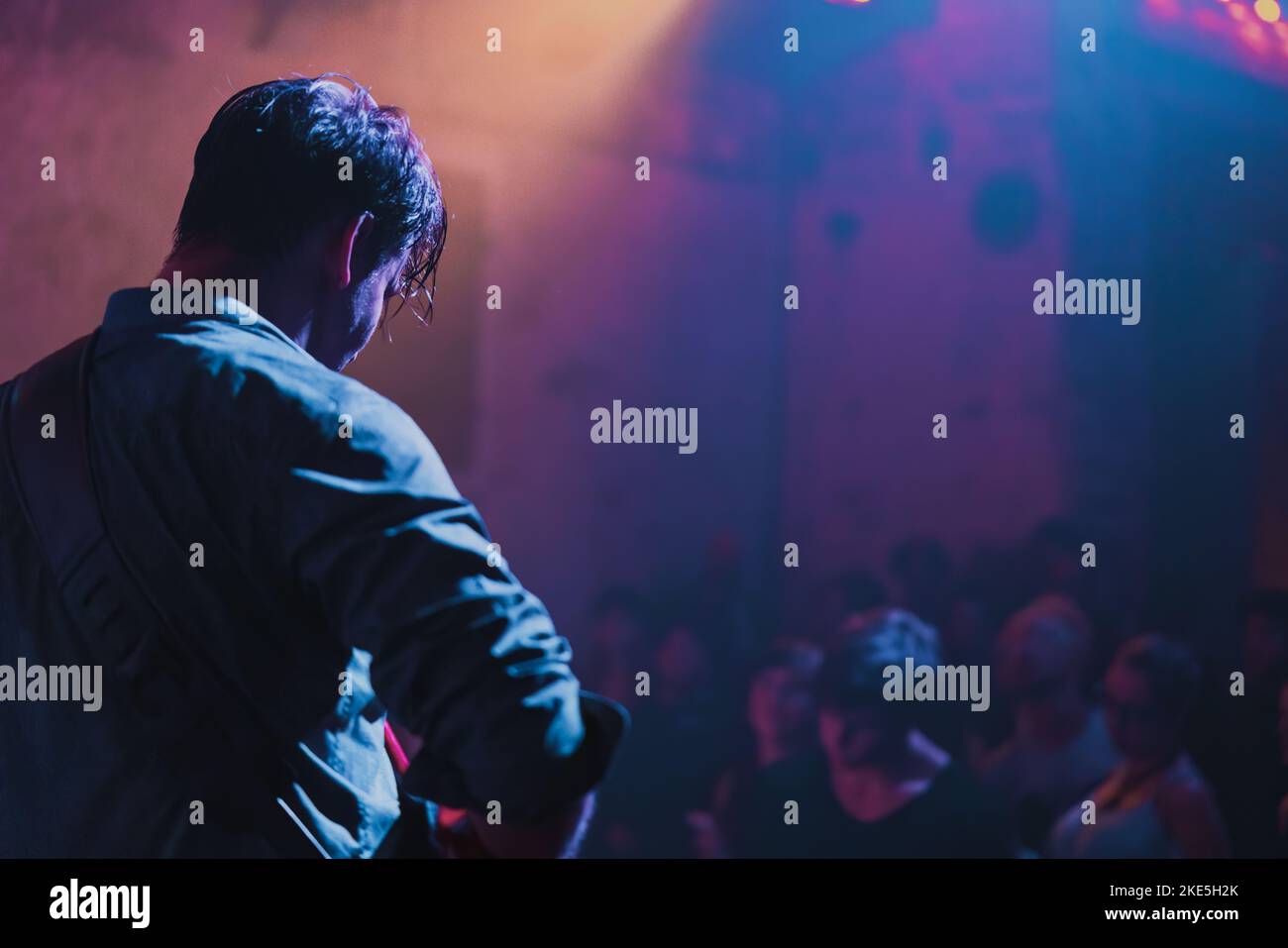 A backside view of a musician guy on the stage performing in front of ...
