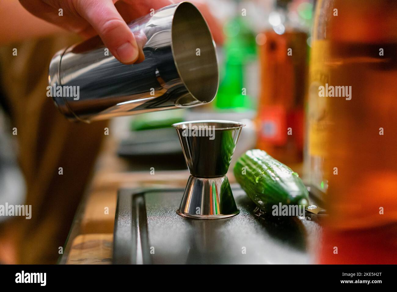 A closeup view of a bartender making a drink with cups on the bar in a ...