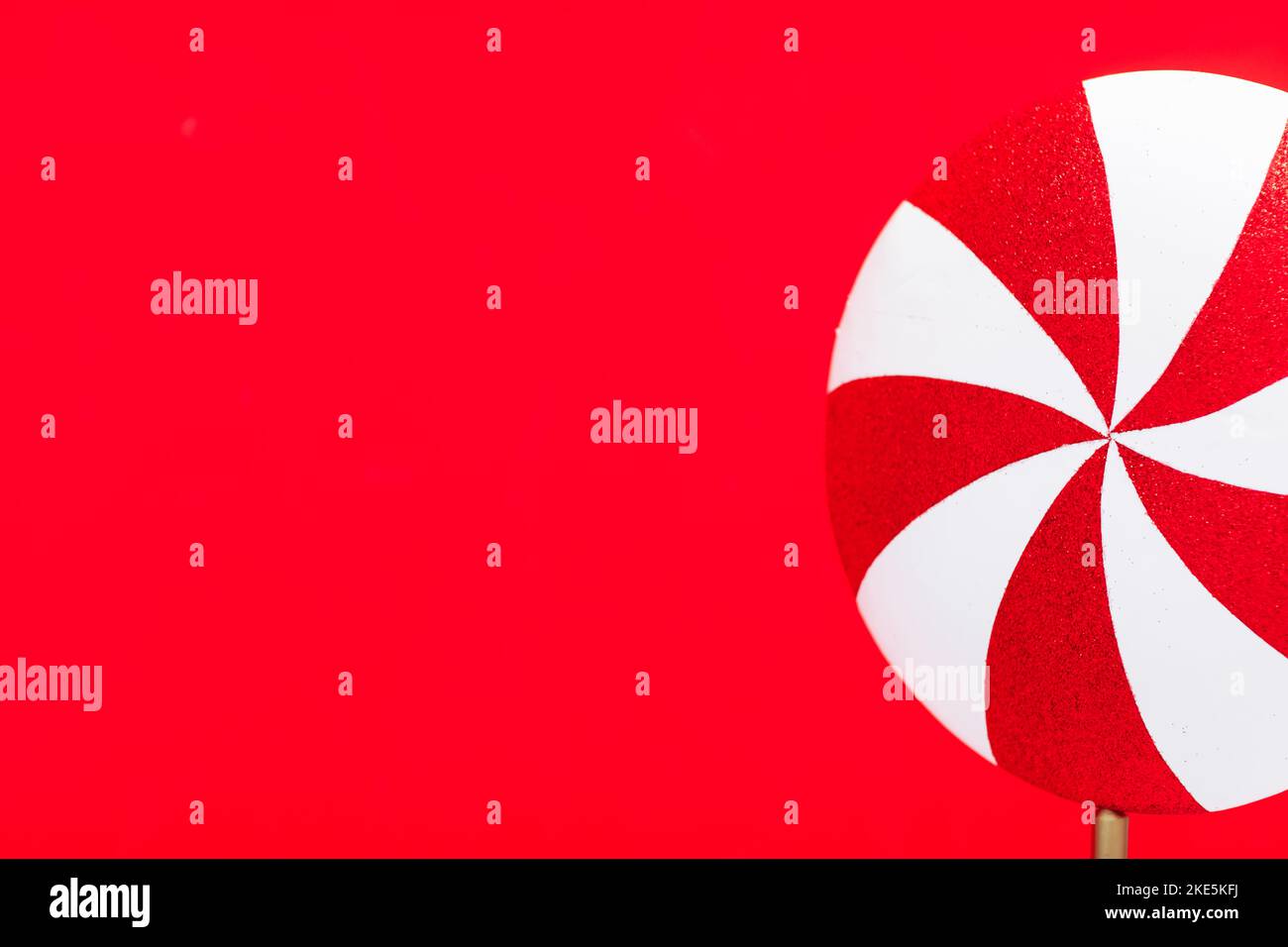 Red-white lollipop swirl on a white stick over red background. Top view ...