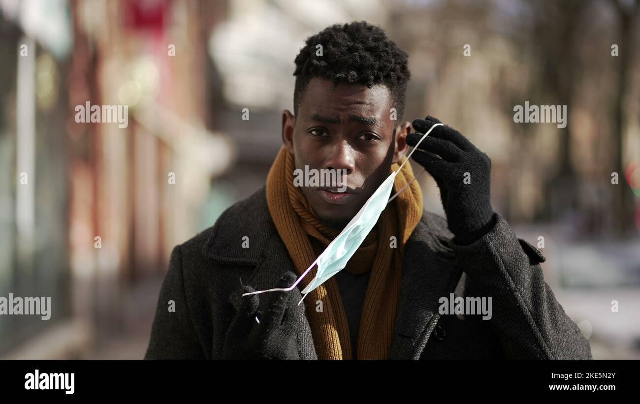 Black man putting covid-19 face mask while walking outside in city ...