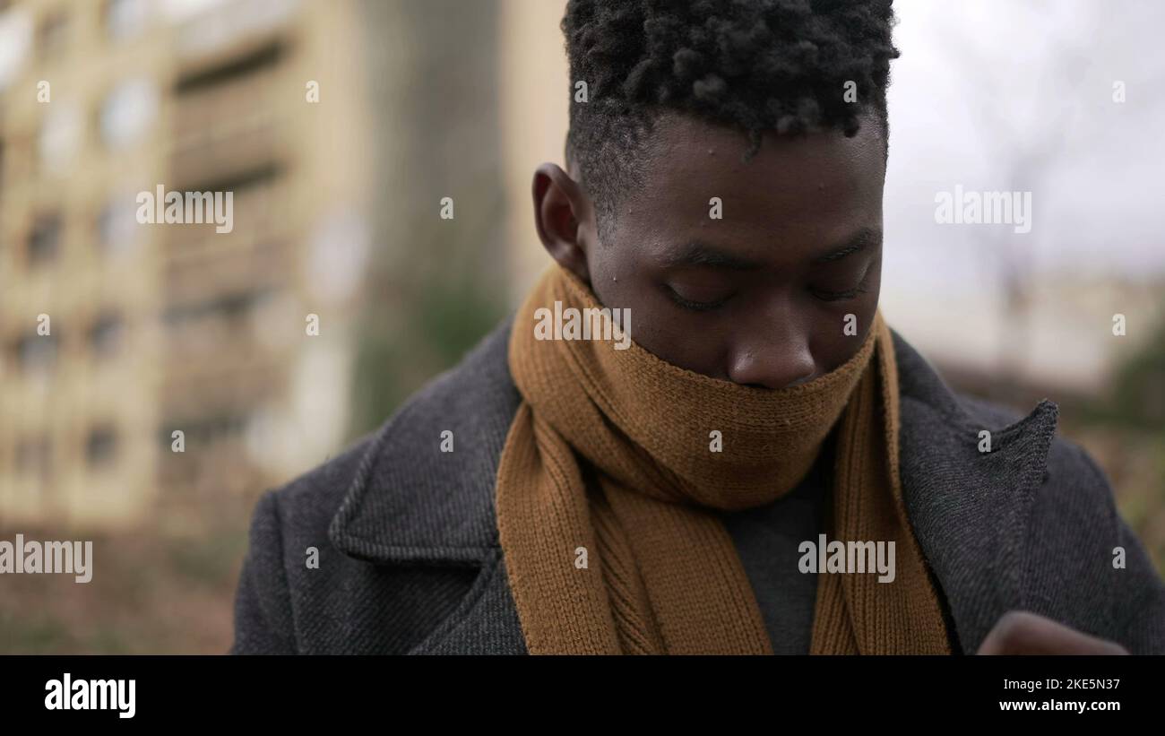 Black man putting scarf outdoors in winter season. African guy ...